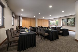 Uma sala de conferências com várias mesas e cadeiras, equipada com garrafas de água e placas de identificação.