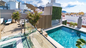 Piscina no terraço com água azul cristalina, rodeada por espreguiçadeiras e um guarda-corpo de vidro.