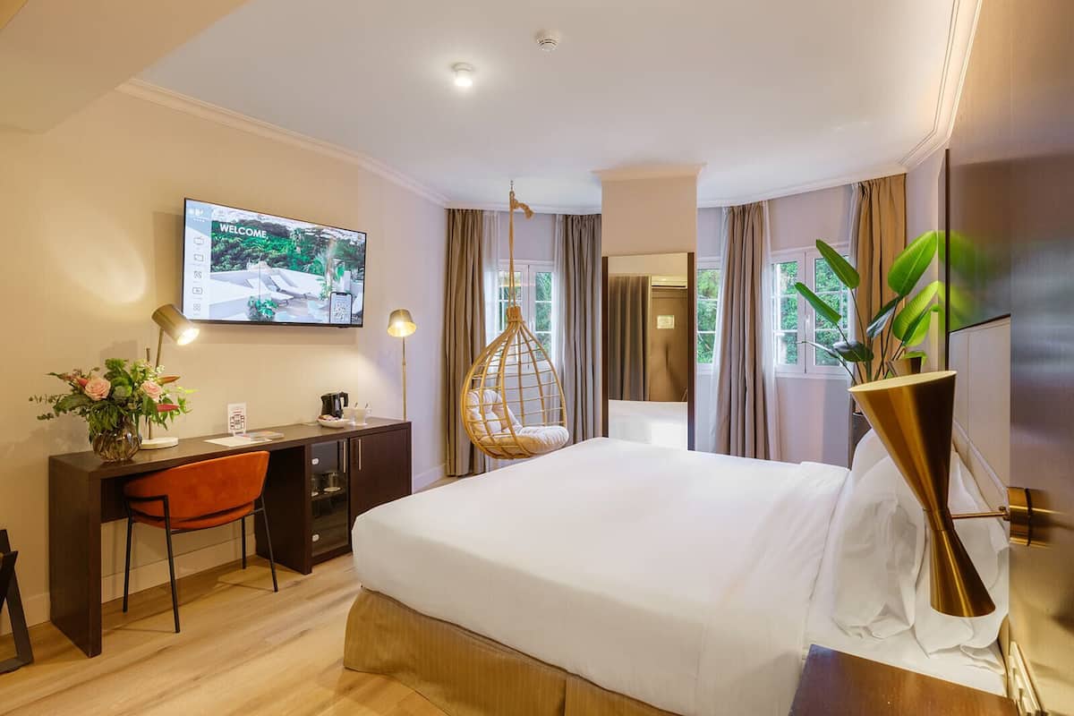 Quarto de hotel moderno com cama, escrivaninha, cadeira, TV e poltrona suspensa.