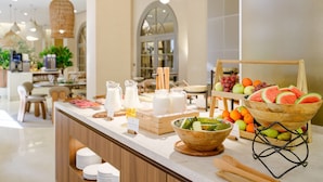 Um buffet de café da manhã com diversas frutas, sucos e uma ilha de saladas.
