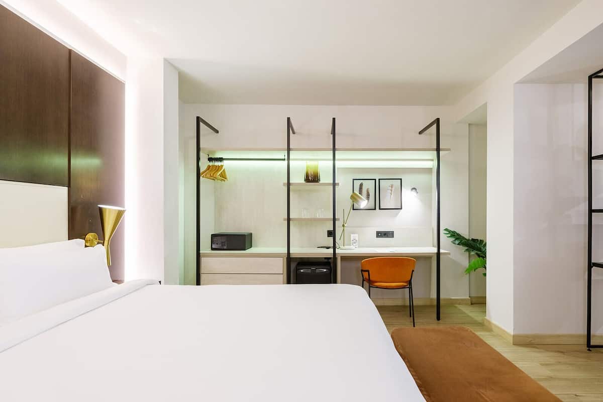 Quarto de hotel moderno com uma cama grande, uma mesa de trabalho com cadeira e um pequeno espaço de estar.