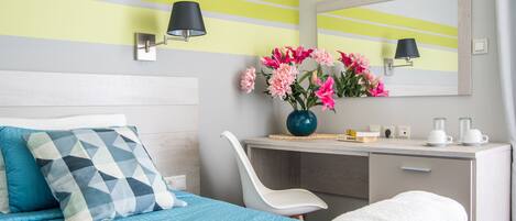 Quarto de hotel com cama, escrivaninha, cadeira, vaso com flores e espelho.