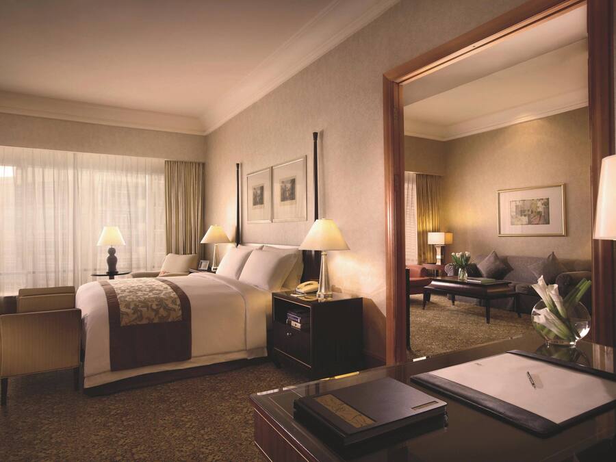 Quarto de hotel com cama grande, duas mesas de cabeceira com luminárias, escrivaninha com cadeira, espelho e vista para a cidade pela janela.