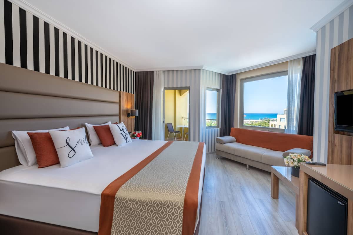 Quarto de hotel com uma cama grande, um sofá, uma televisão e vista para o mar.