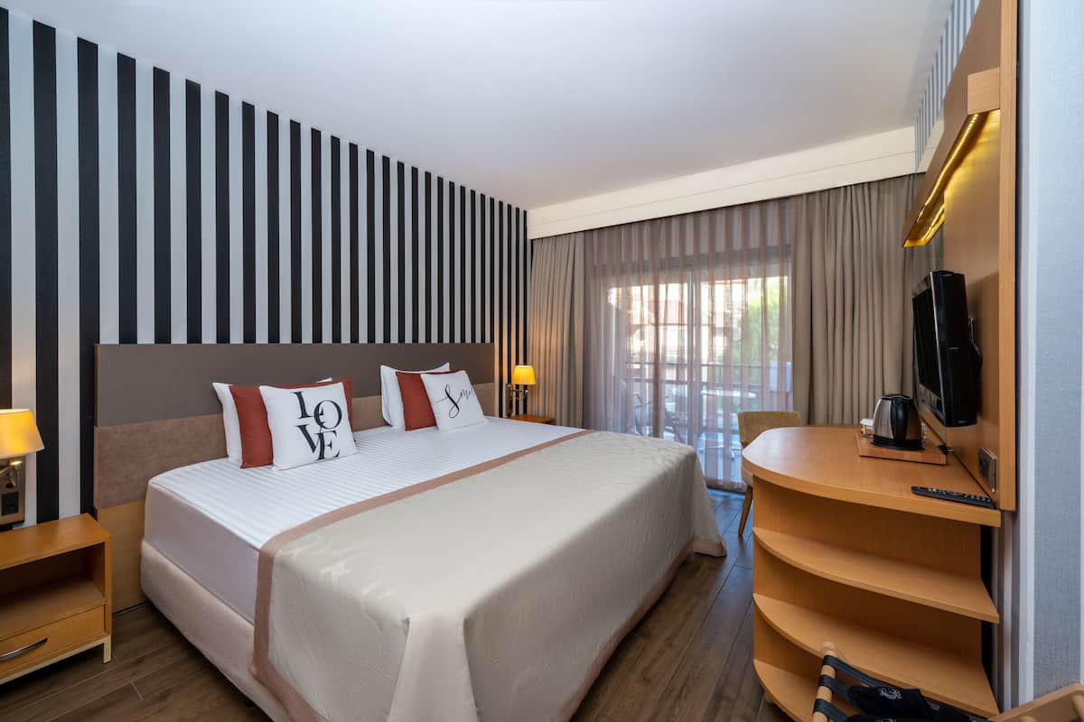 Quarto de hotel com uma cama grande, uma escrivaninha com televisão e vista para o exterior.