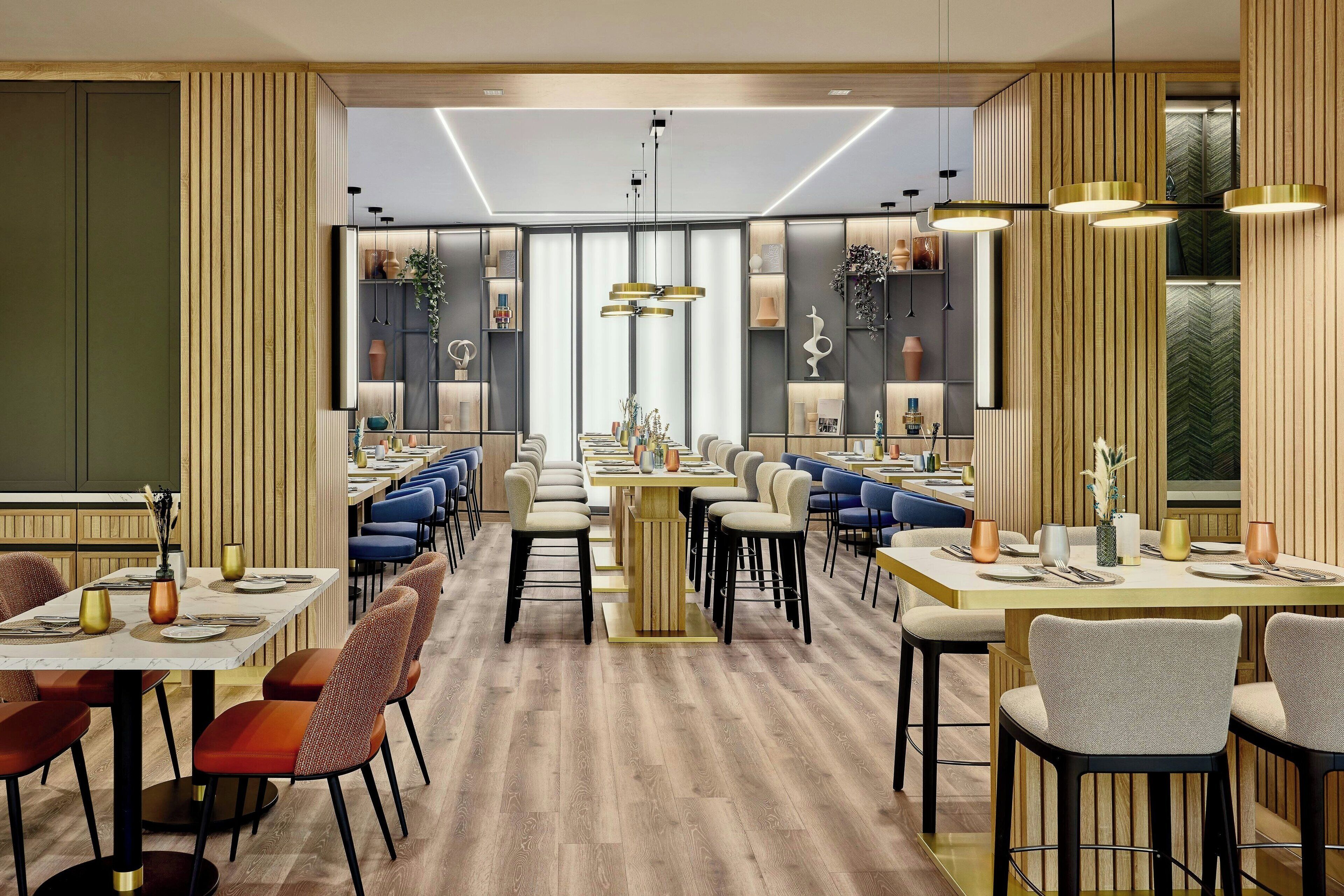 Restaurante moderno com várias mesas e cadeiras, painéis de madeira e iluminação pendente.