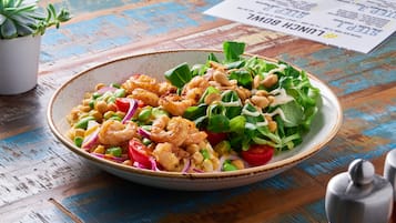 Uma tigela de camarão e salada sobre uma mesa de madeira, com um menu ao fundo.
