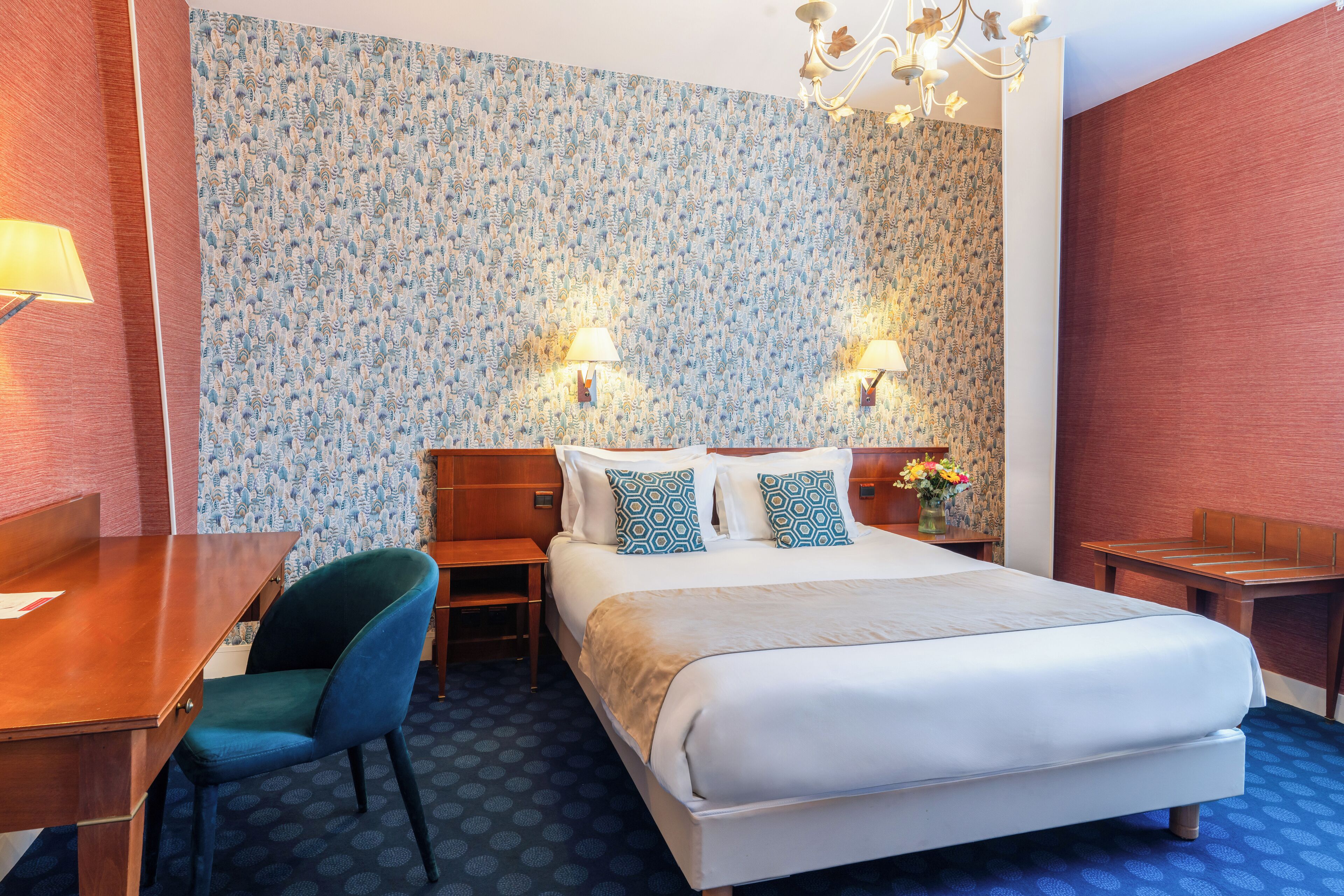 Quarto de hotel com uma cama grande, duas mesas de cabeceira, uma escrivaninha, uma cadeira e papel de parede estampado.