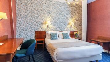Quarto de hotel com uma cama grande, duas mesas de cabeceira, uma escrivaninha, uma cadeira e papel de parede estampado.