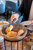 Uma tigela de madeira com croissants numa estante, um frasco de vidro com canudo, e um prato com colher.
