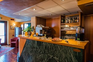 Uma área de bar com bancada de mármore, máquina de café e diversas garrafas e copos nas prateleiras.