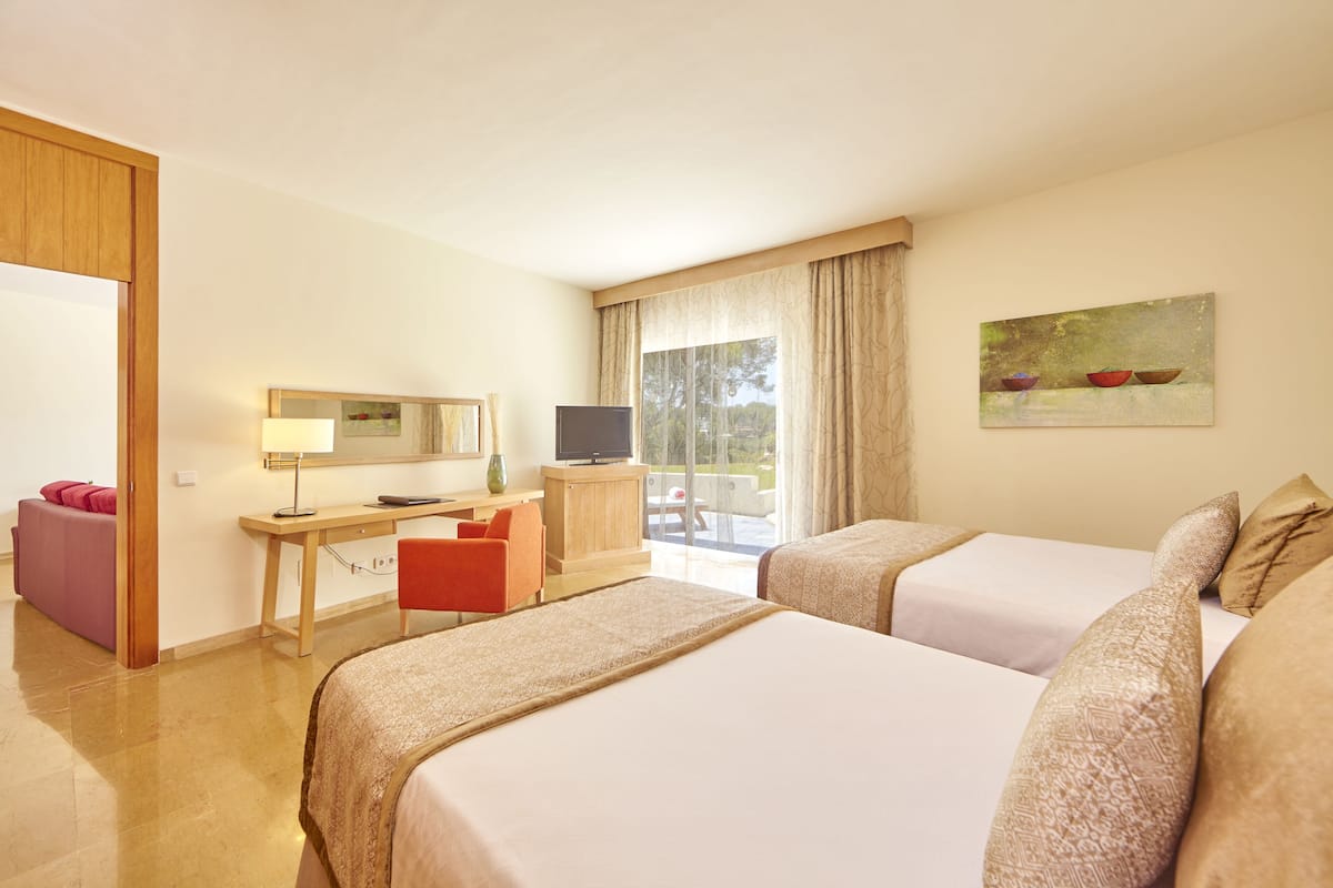 Quarto de hotel com duas camas, uma escrivaninha, uma cadeira, televisão e janela com cortinas.