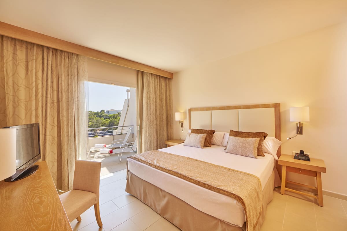 Quarto de hotel com cama grande, televisão, escrivaninha e vista para o exterior.