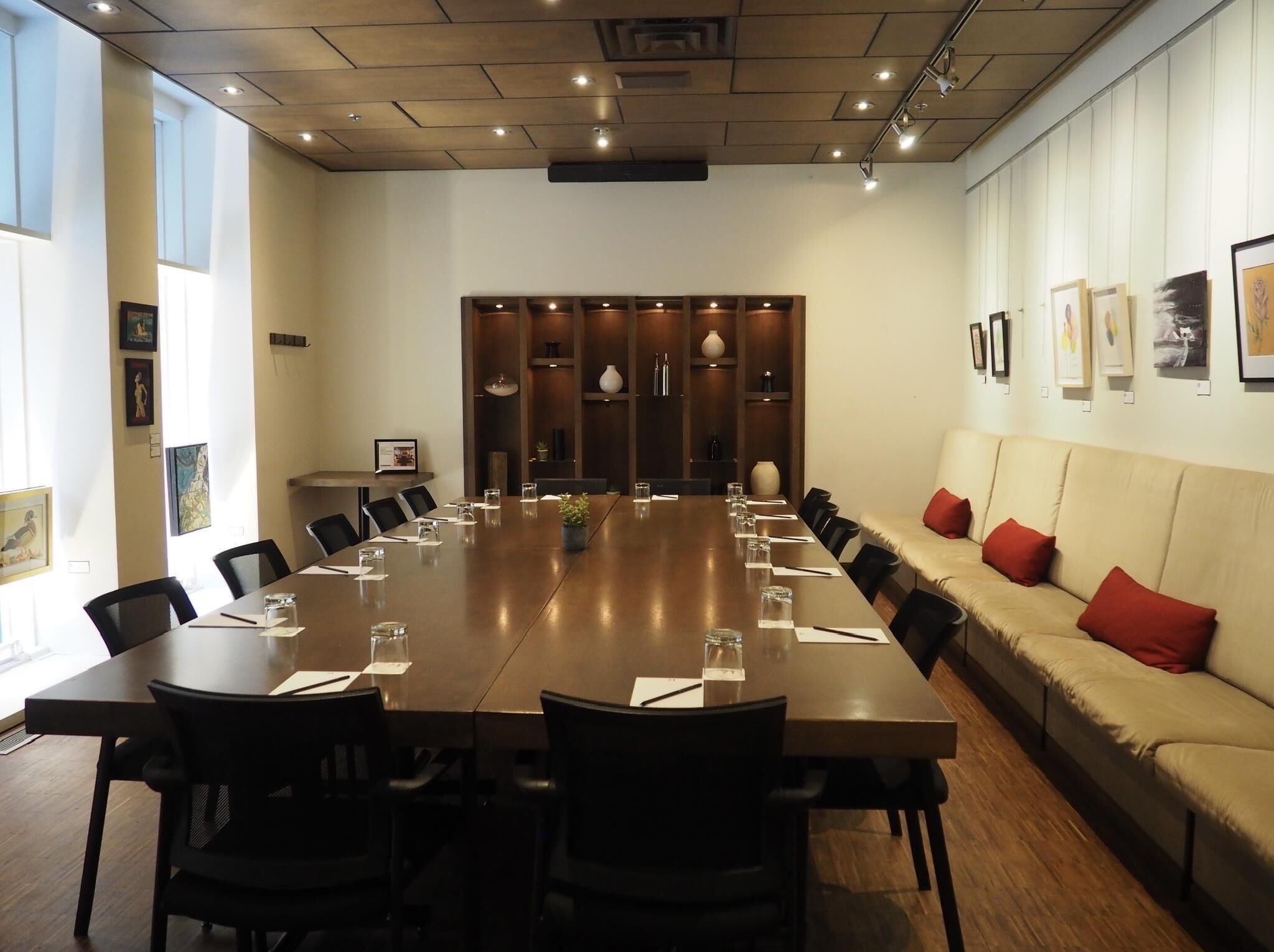 Uma sala de conferências com uma mesa comprida, cadeiras pretas, um sofá bege com almofadas vermelhas e obras de arte emolduradas nas paredes.