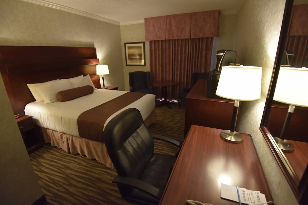 Quarto de hotel com cama, escrivaninha, cadeira, abajur, telefone e espelho.