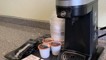 Uma cafeteira em uma bancada com quatro copos descartáveis e um pacote de cápsulas de café.
