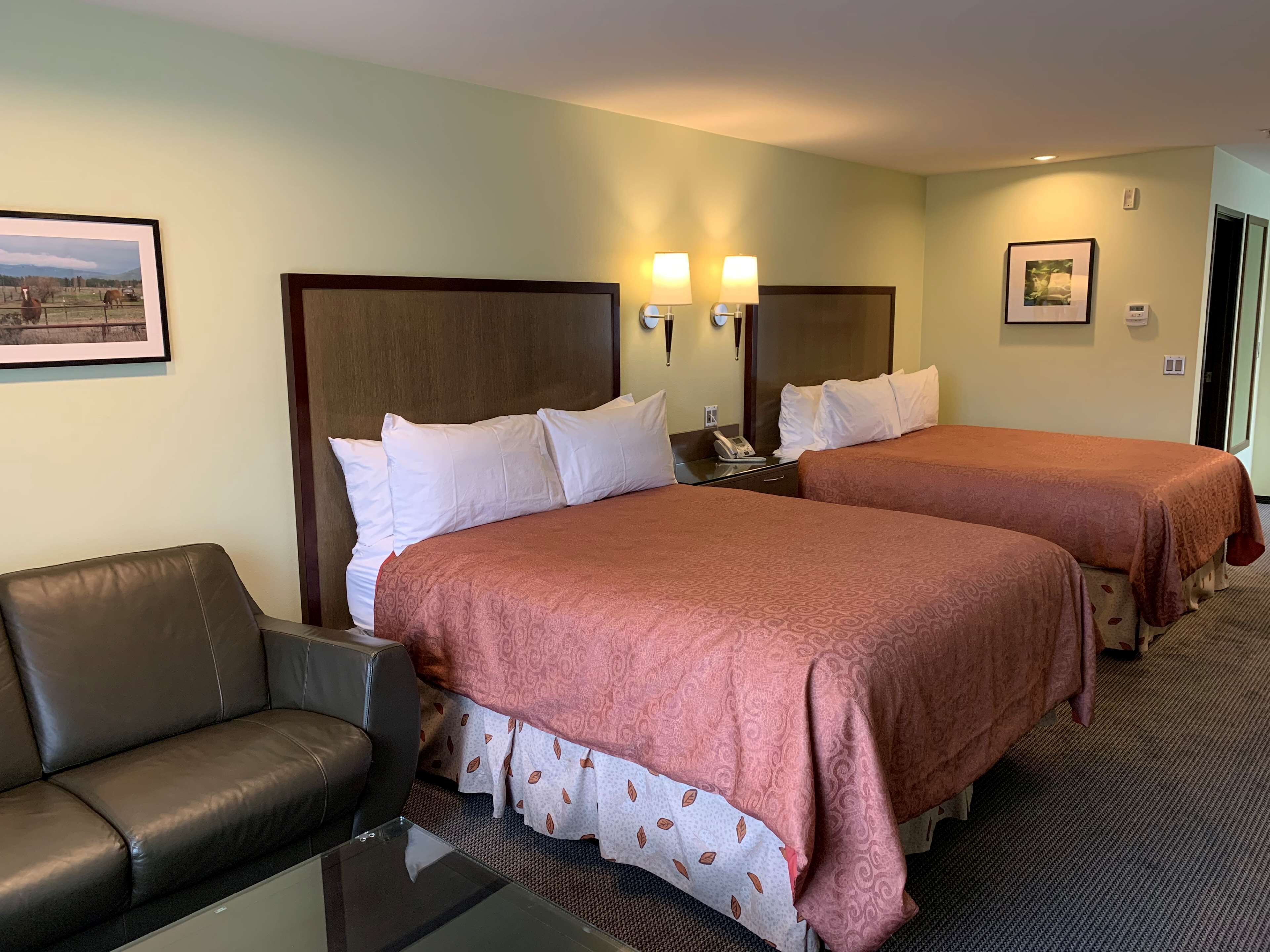 Quarto de hotel com duas camas, um sofá, uma escrivaninha e uma mesinha de cabeceira.
