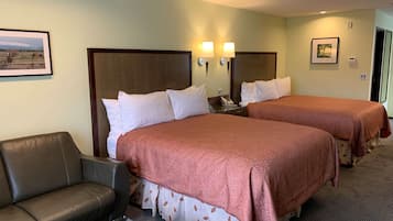 Quarto de hotel com duas camas, um sofá, uma escrivaninha e uma mesinha de cabeceira.
