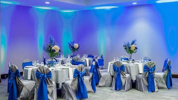 Uma sala de banquetes com mesas redondas, cadeiras com fitas azuis e arranjos florais.
