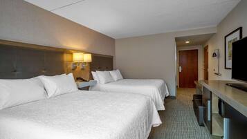 Quarto de hotel com duas camas, uma escrivaninha com televisão e porta para um corredor.