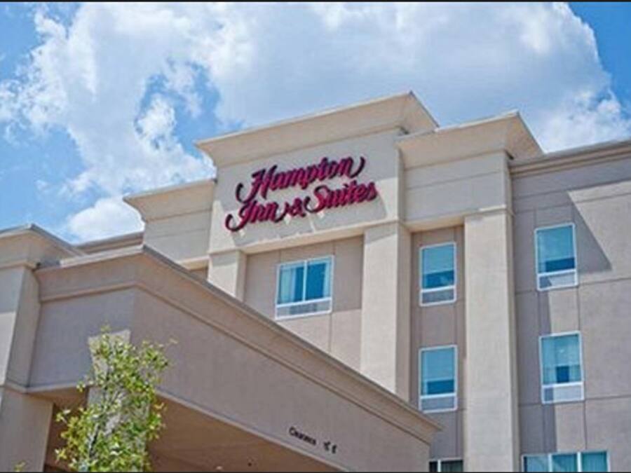Edifício do Hampton Inn & Suites com placa visível, telhado plano e várias janelas.