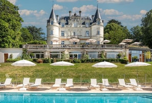 Um edifício grande e histórico com piscina, área de estar ao ar livre e guarda-sóis.