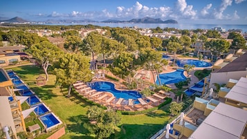 Um resort com várias piscinas, vegetação exuberante e vista para o mar e montanhas.