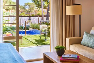 Uma sala de estar moderna com um sofá, uma mesa de centro com livros, um abajur e vista para uma piscina e jardim.