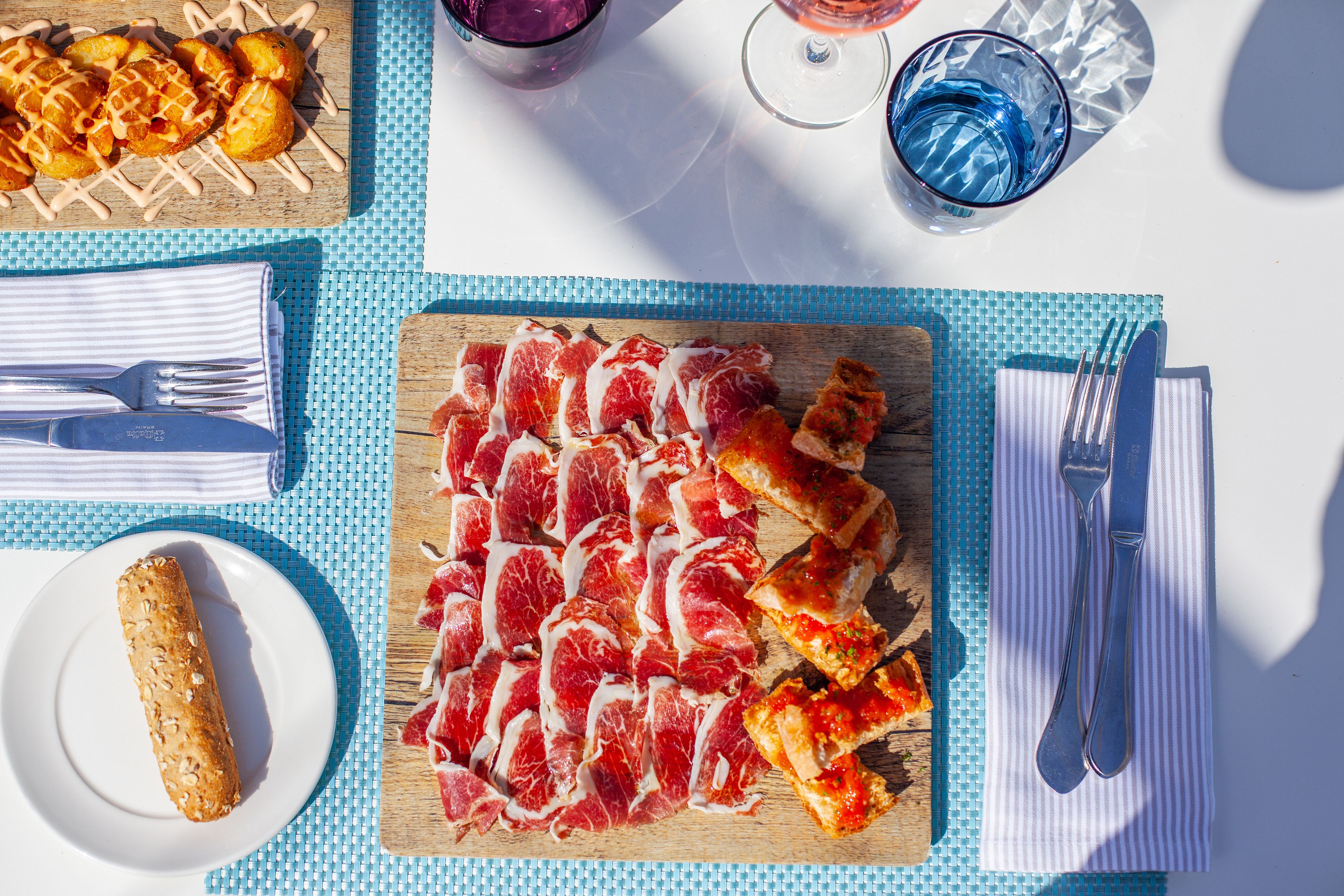 Uma mesa com diversos alimentos, incluindo carnes fatiadas e pão, dispostos sobre um jogo americano azul.