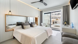Quarto de hotel moderno com uma cama grande, um ventilador de teto, uma televisão e vista para a fachada do edifício.