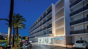 Um hotel moderno com vários andares, entrada coberta e palmeiras em primeiro plano.
