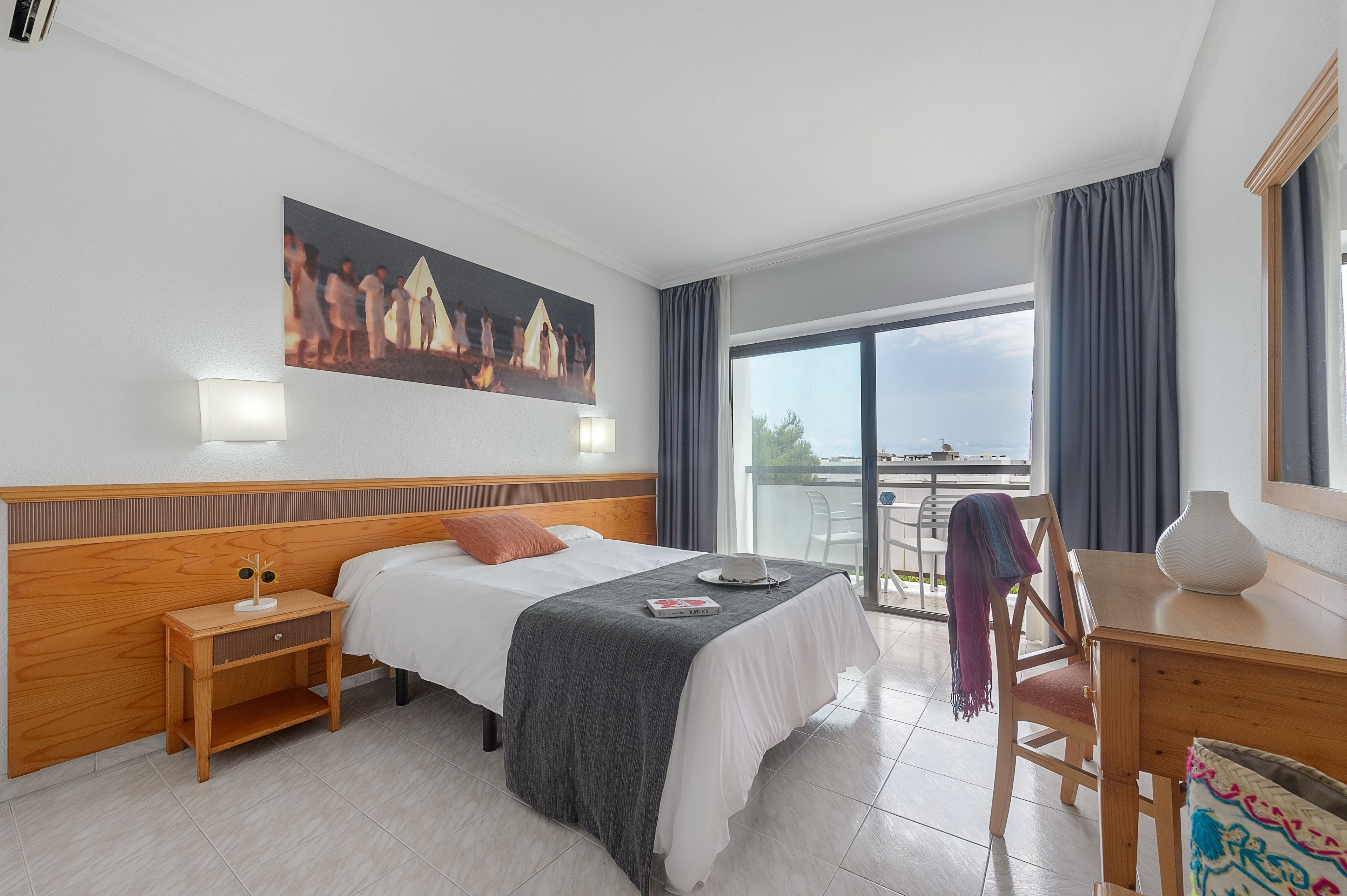 Quarto de hotel com cama, mesa de cabeceira, luminária e um quadro na parede.