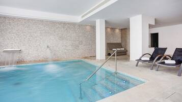 Piscina com piso de azulejos, um recurso aquático e duas espreguiçadeiras.