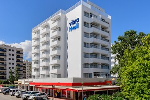 Um edifício moderno de vários andares com varandas, um letreiro 'Vibra Tivoli' e serviço de 'Rent a Car'.