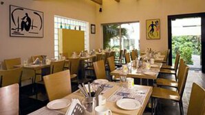 Restaurante com mesas montadas para refeições, cadeiras e obras de arte nas paredes.