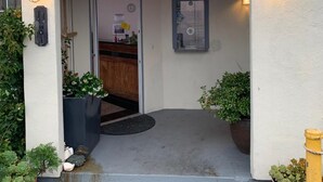 Entrada de um edifício moderno com um arco convidativo, uma receção e duas plantas em vasos de cada lado.