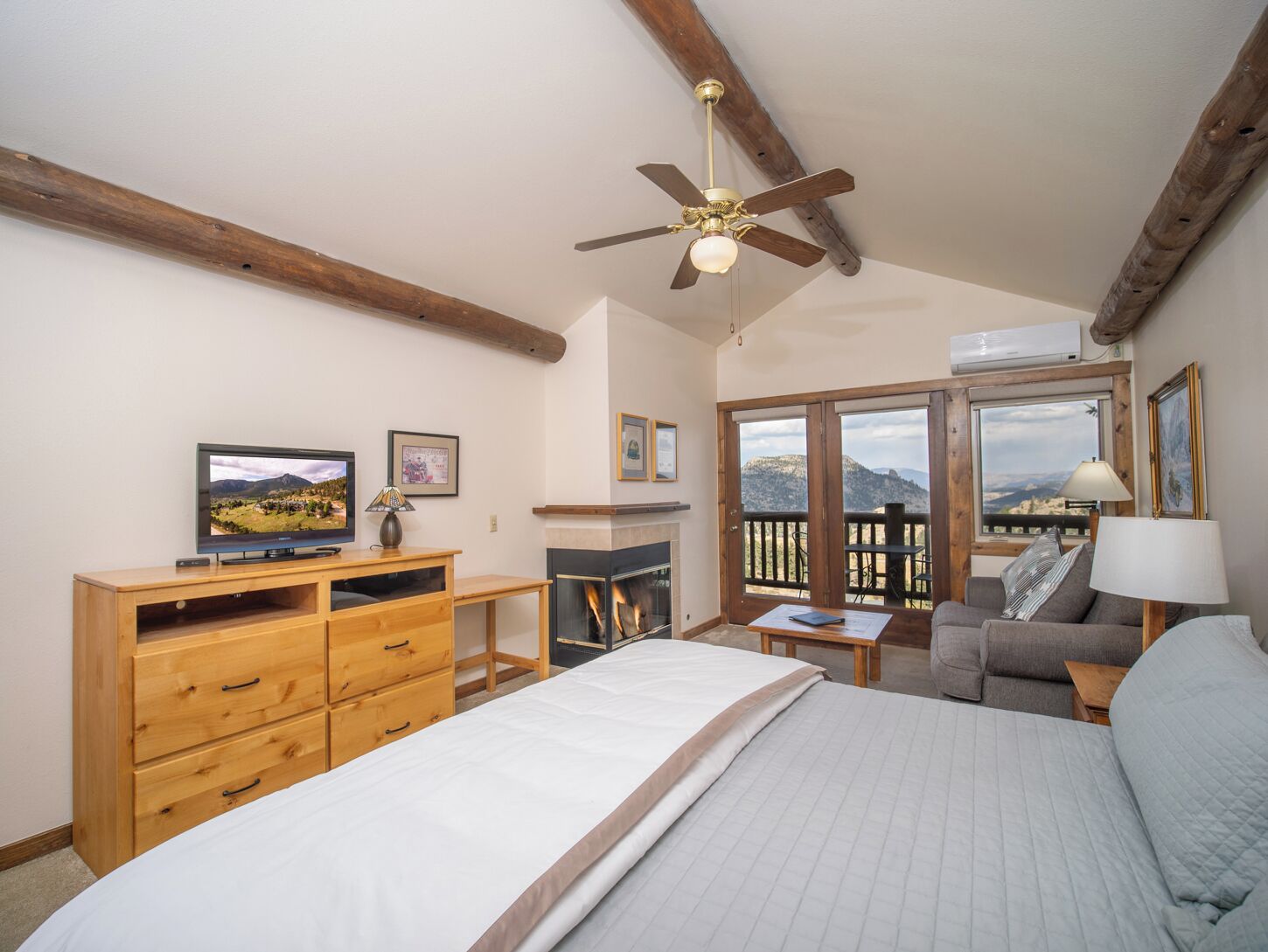 Quarto com cama, cómoda de madeira, televisão, lareira e varanda com vista.