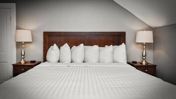 Cama bem arrumada com cabeceira de madeira, ladeada por duas mesas de cabeceira com abajures.