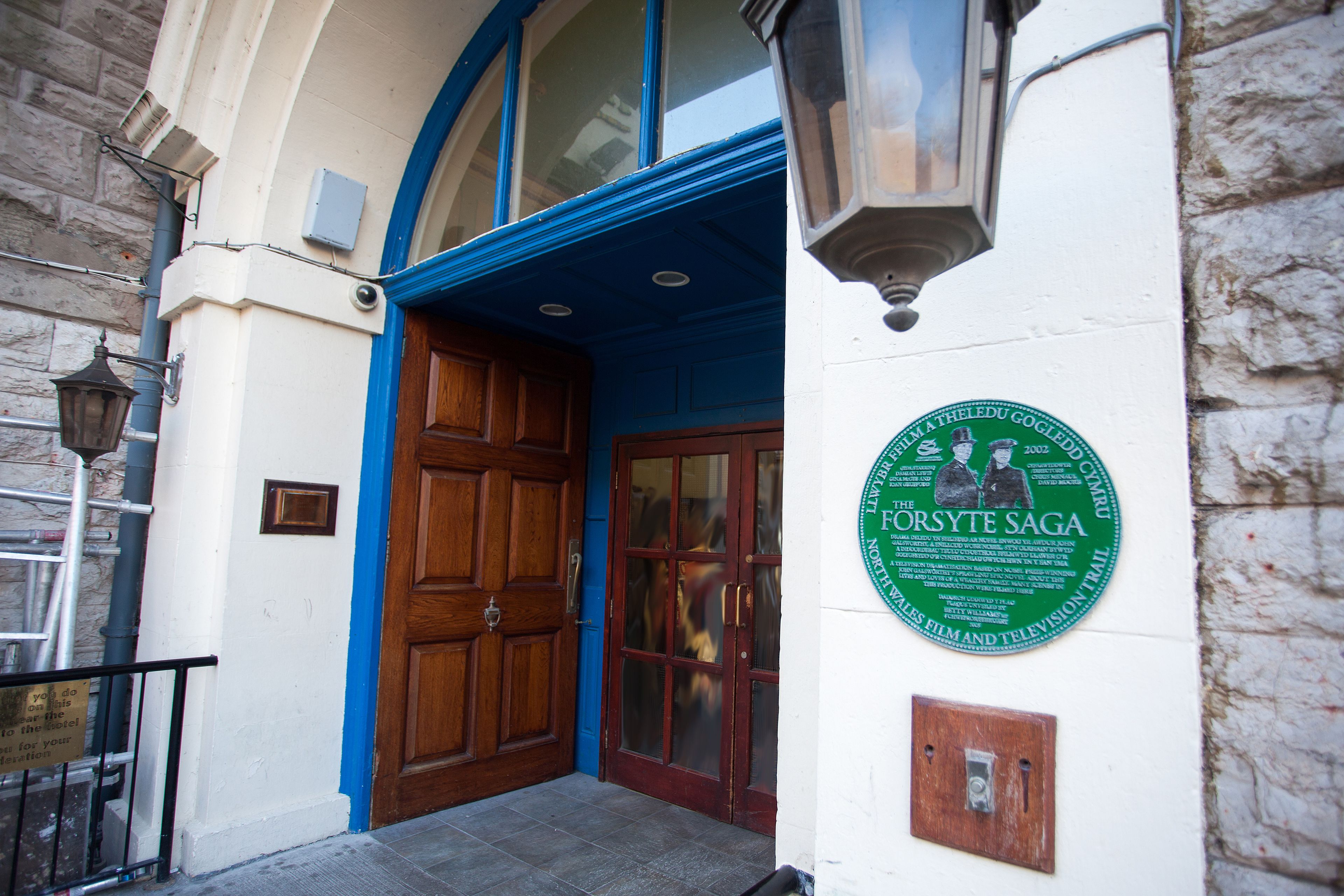 Entrada de um edifício com porta azul, placa e luminária.