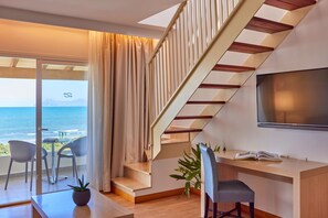 Sala de estar moderna com escada, televisão, escrivaninha e vista para o mar.