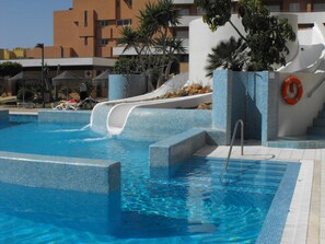Uma piscina com escorrega, espreguiçadeiras e boia.