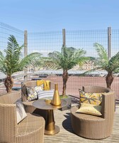 Terraço no telhado com móveis de vime, uma mesa redonda e palmeiras.