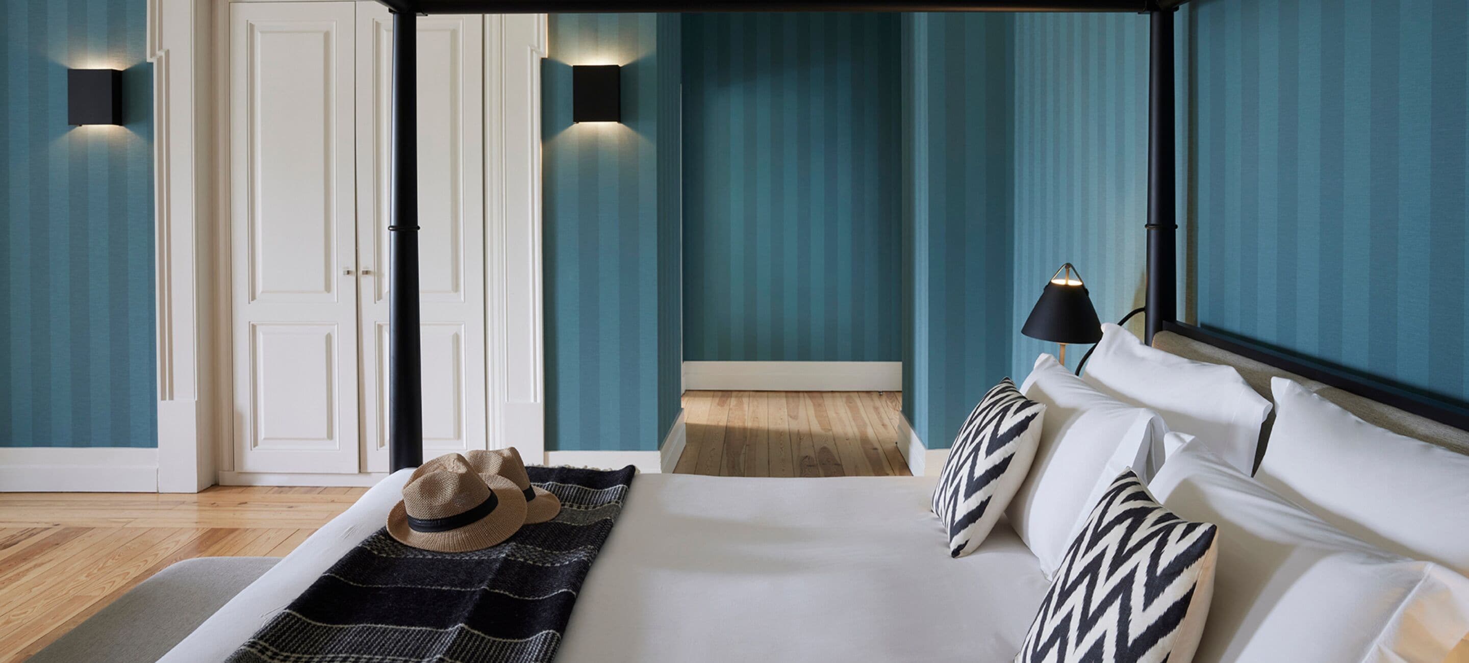 Quarto de hotel com cama, mesa de cabeceira, luminária e janela.