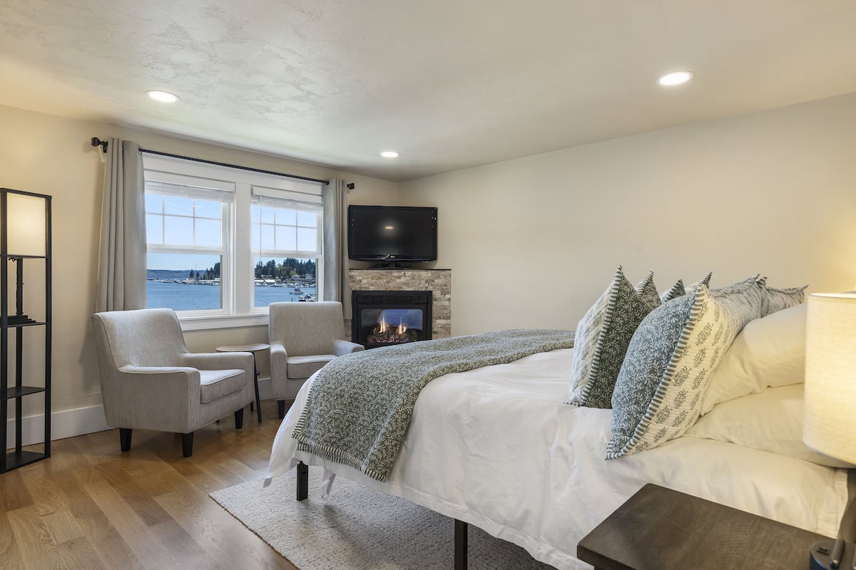 Quarto com lareira, cama, televisão e vista para o exterior.