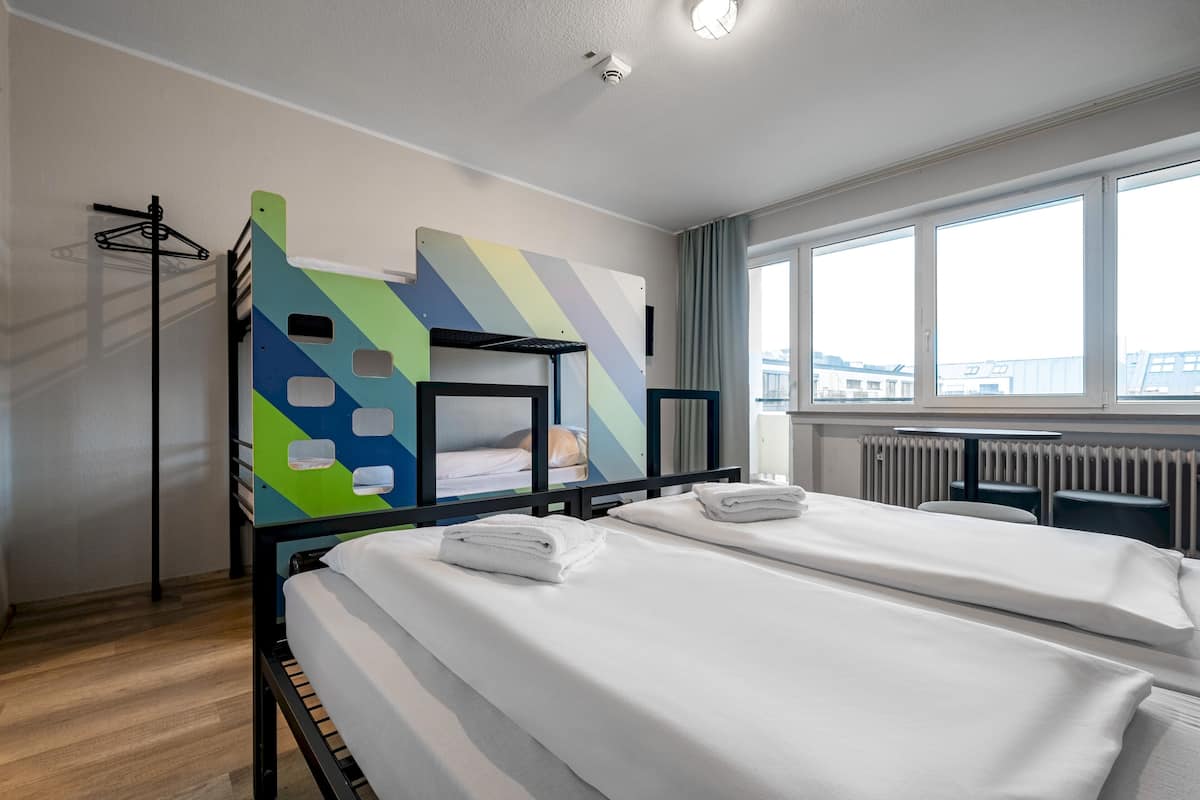 Quarto de hotel moderno com beliches, radiador, janela com vista e cabideiro.