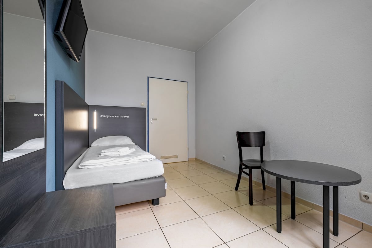 Quarto de hotel moderno com uma cama, uma mesa pequena, uma cadeira e uma televisão.