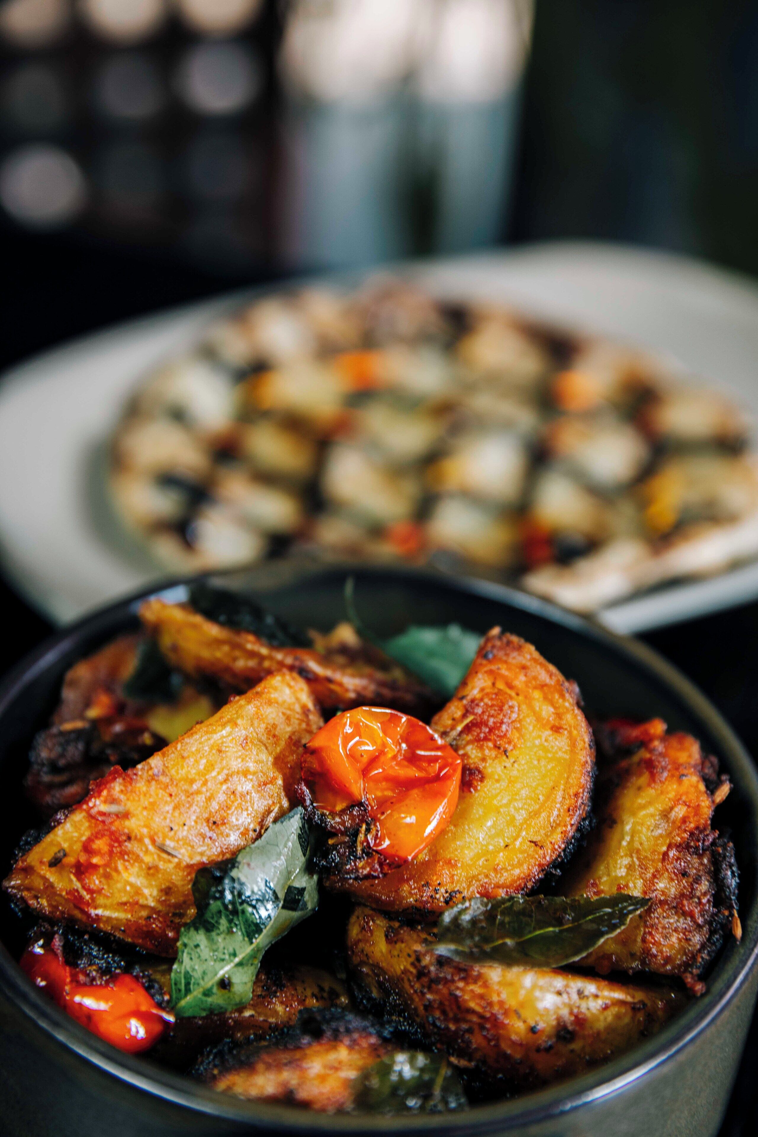Uma tigela de batatas assadas decorada com ervas e uma fatia de tomate.
