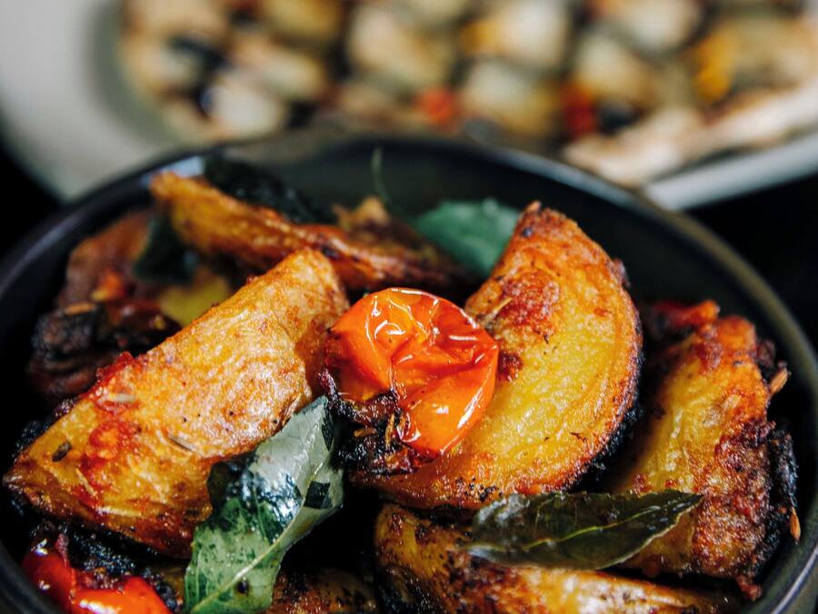 Uma tigela de batatas assadas decorada com ervas e uma fatia de tomate.