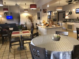 Um restaurante com área de bar, mesas, cadeiras e uma tela de televisão.