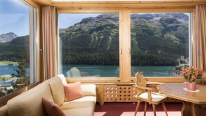 Um quarto aconchegante com uma grande janela que oferece vista para as montanhas, uma mesa de madeira com uma cadeira e um sofá com almofadas.